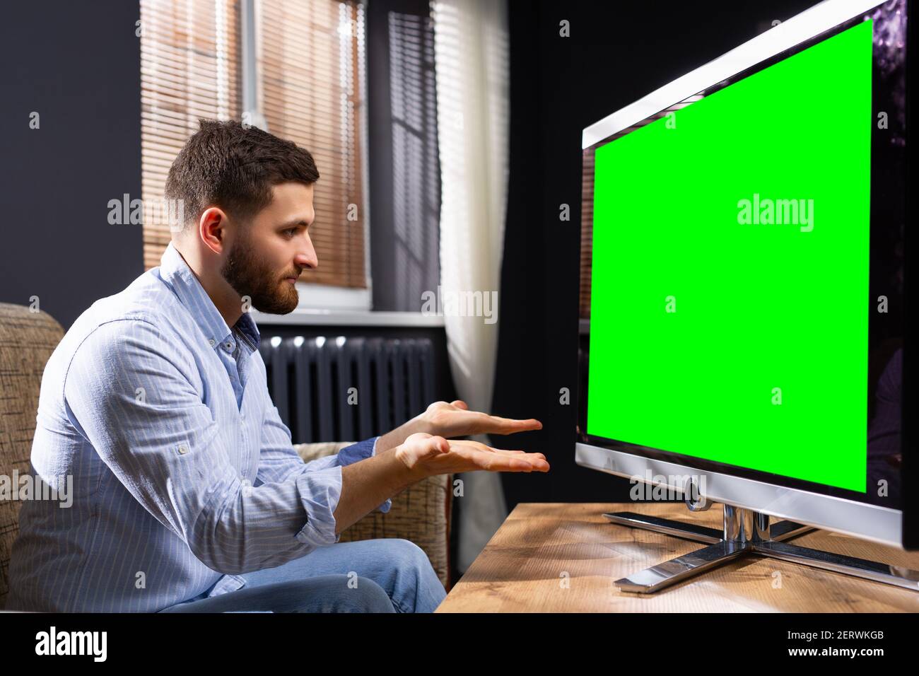 A young man gesticulating in front of TV at home, confused, does not ...