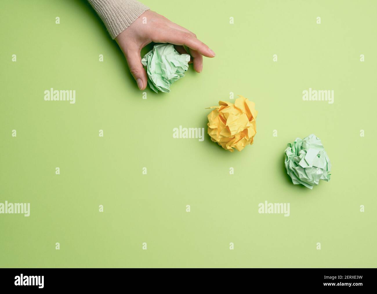 three crumpled balls of colored paper on a green background, hand ...