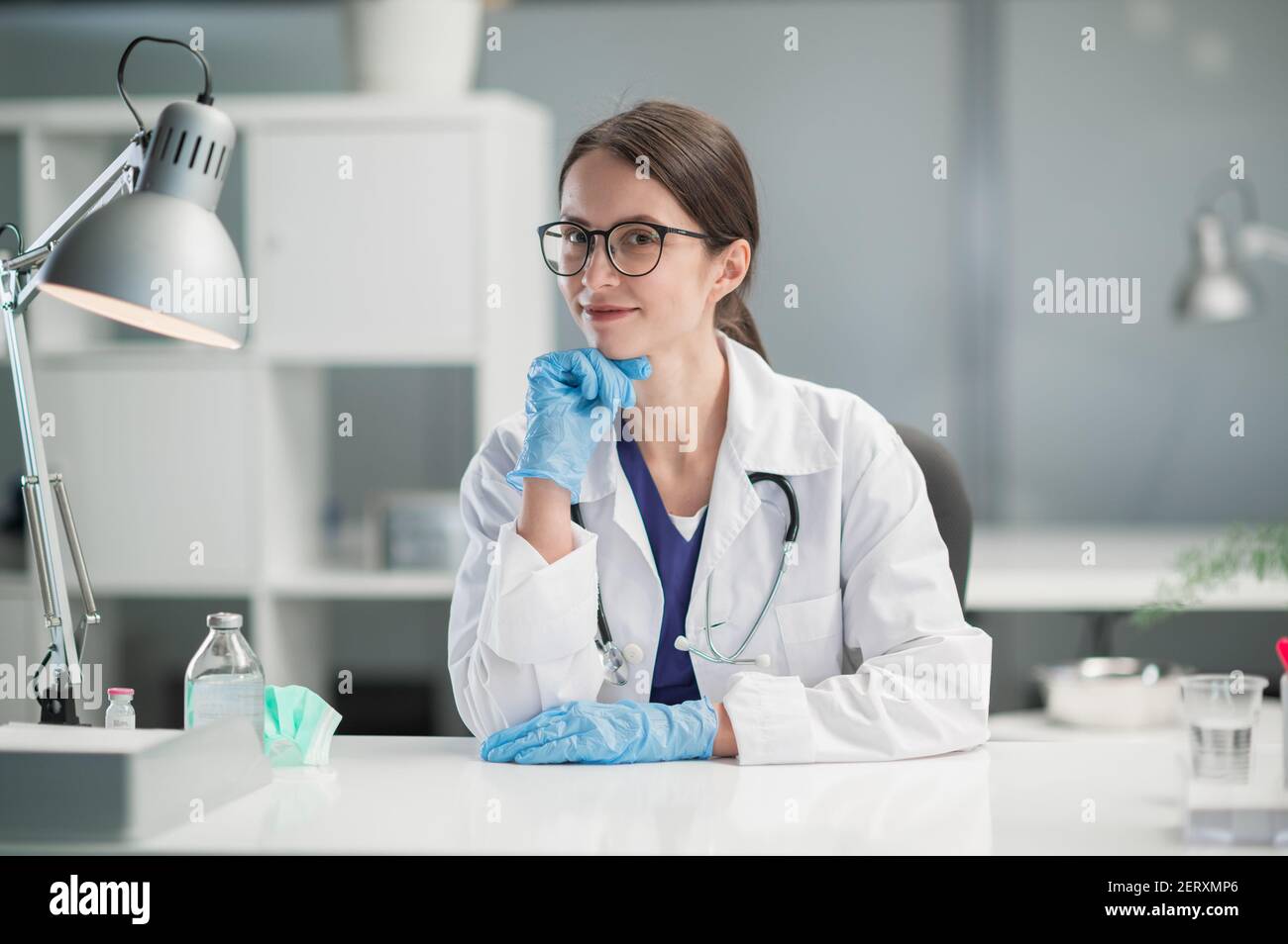 A young female internist is sitting at a desk in her spacious, bright ...