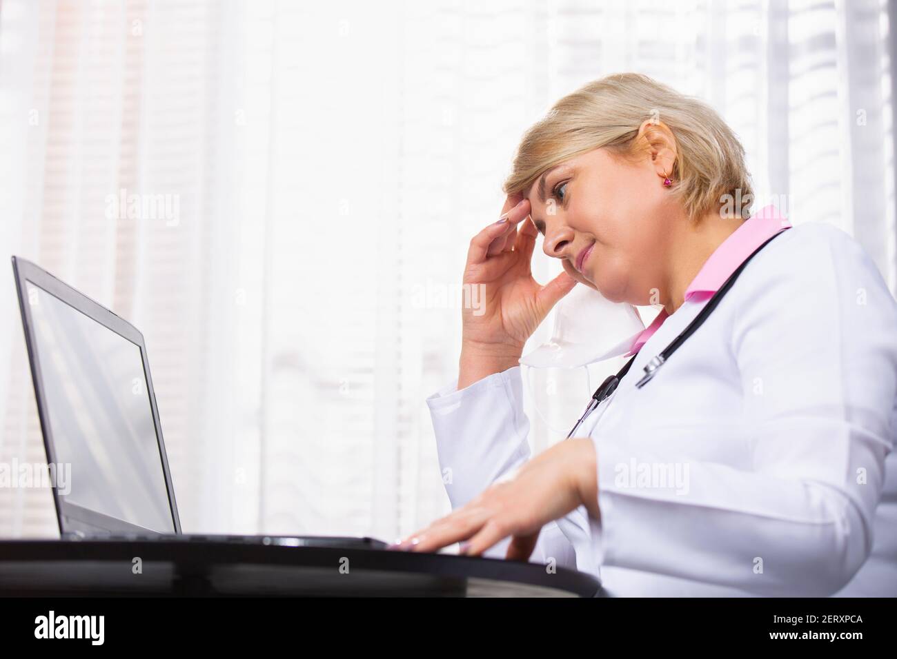Senior woman doctor at the computer in her office holding her head ...