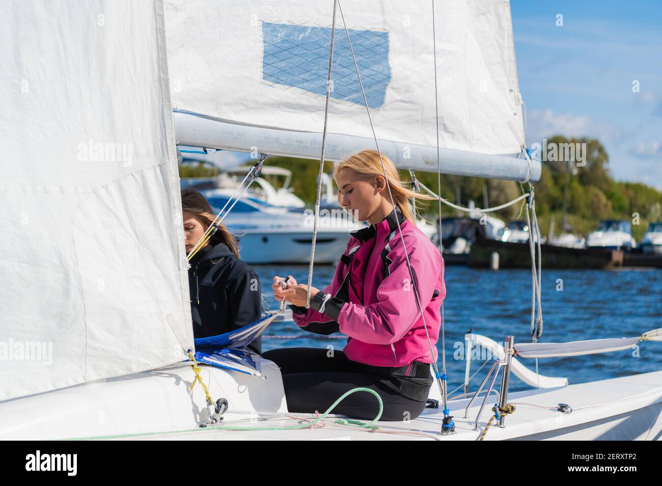 On the pier, two pretty girls pull sails on a boat to participate in a ...