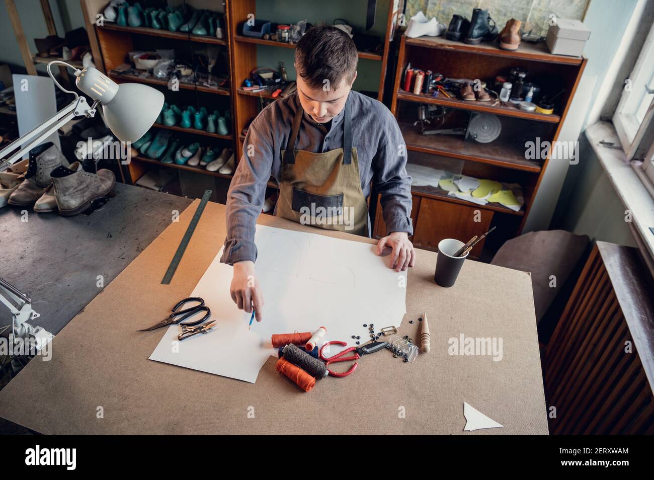 An experienced shoemaker in a shoe production workshop makes a pattern ...