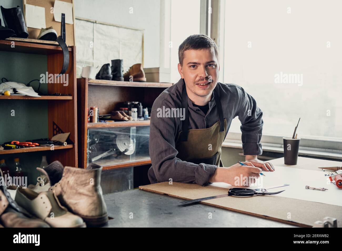 A young shoemaker makes a drawing for a pattern for leather shoes on a ...