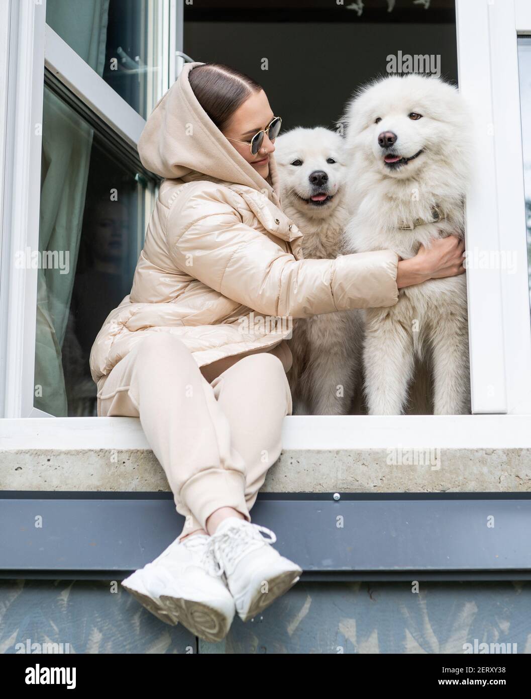 A young beautiful brunette is sitting on the windowsill in the window ...