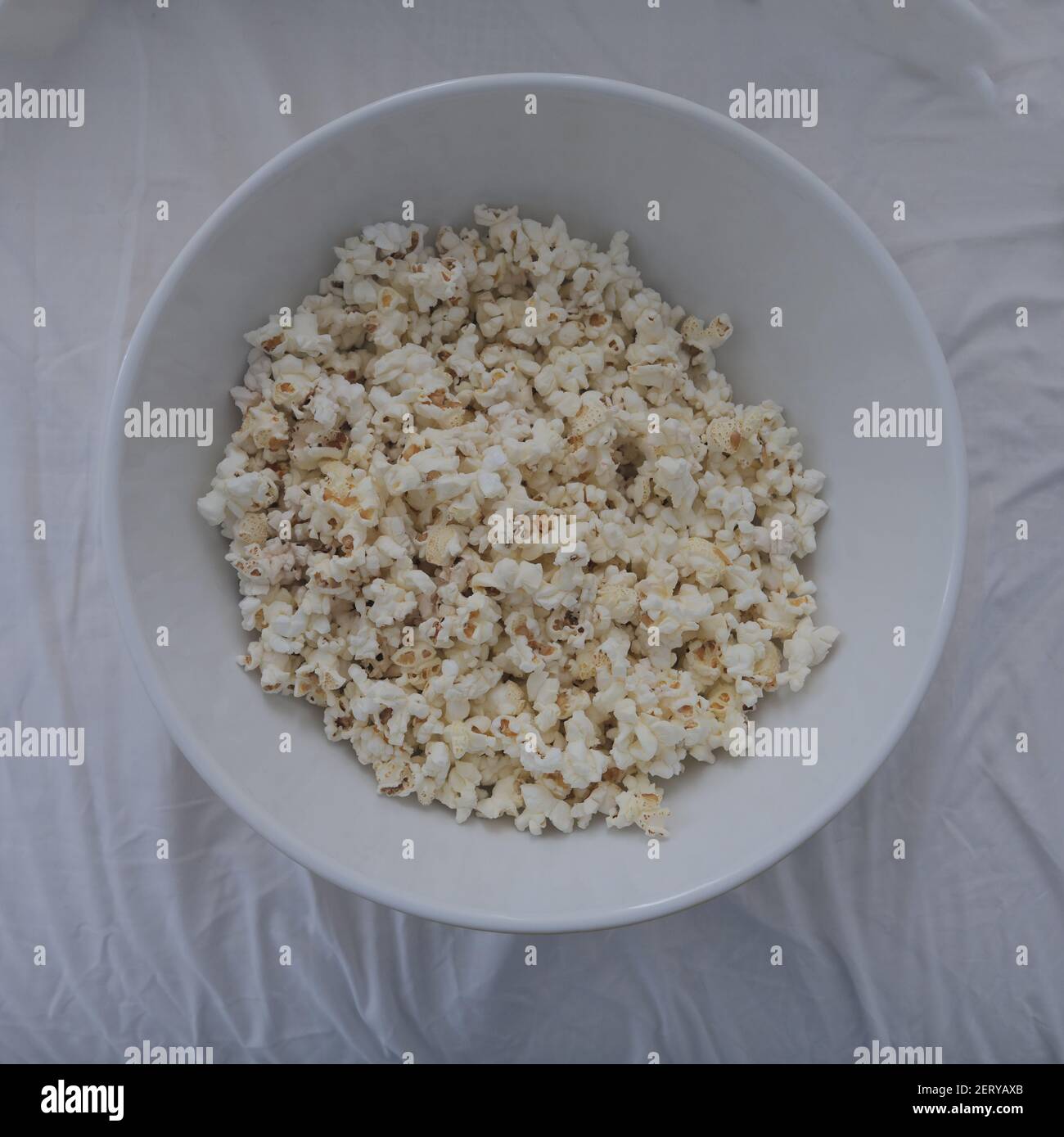 A closeup shot of popcorn in a white bowl on a bed Stock Photo - Alamy
