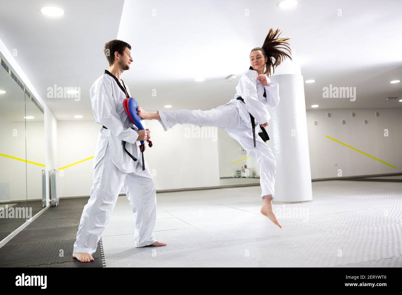 Cute brunette girl doing a leg kick practice while her trainer assists ...