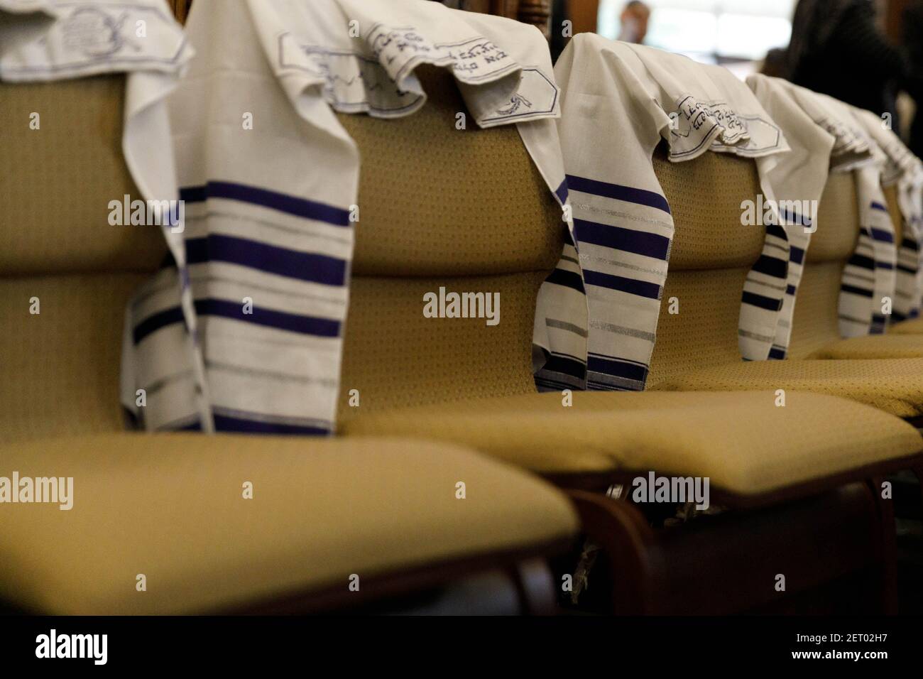 A row of eleven empty chairs, each with a talit, symbolizes the ...