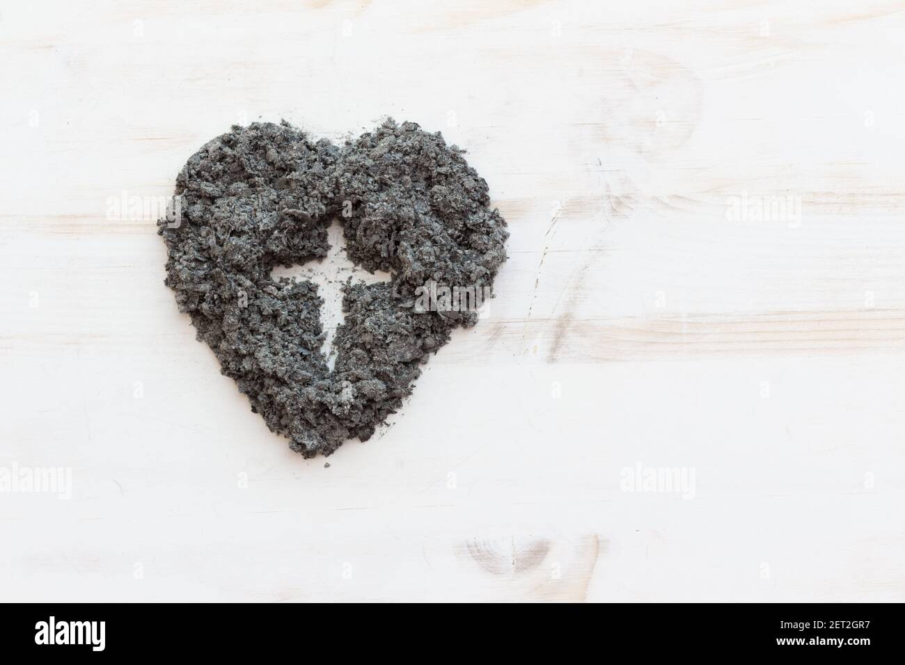 shape of a christian cross in a heart of ash on a white wood background ...