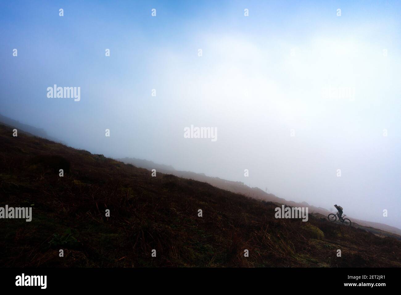 Mountain biker at the bottom of a steep hill cycling uphill in a cloud ...