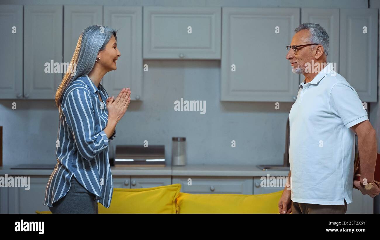 side view of excited asian woman clapping hands near smiling senior ...