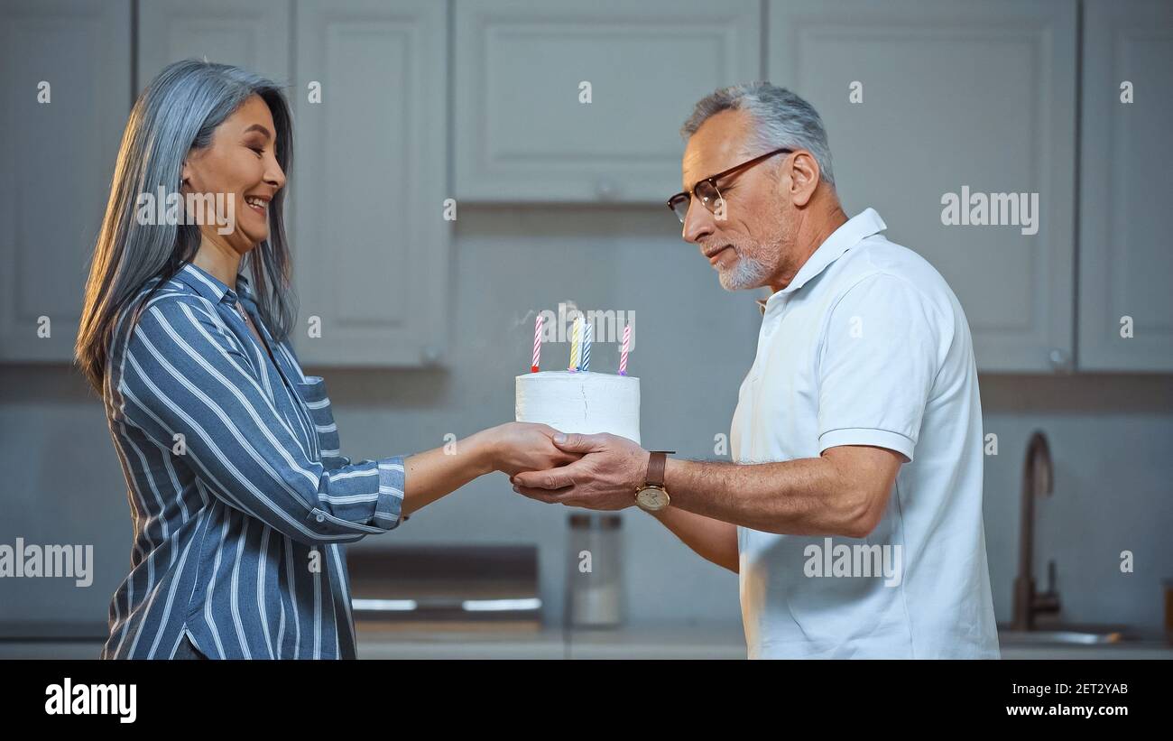 side view of excited asian woman giving birthday cake to senior husband ...