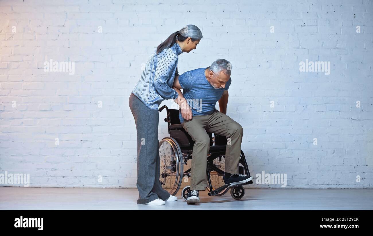 elderly asian woman helping handicapped husband to sit in wheelchair ...