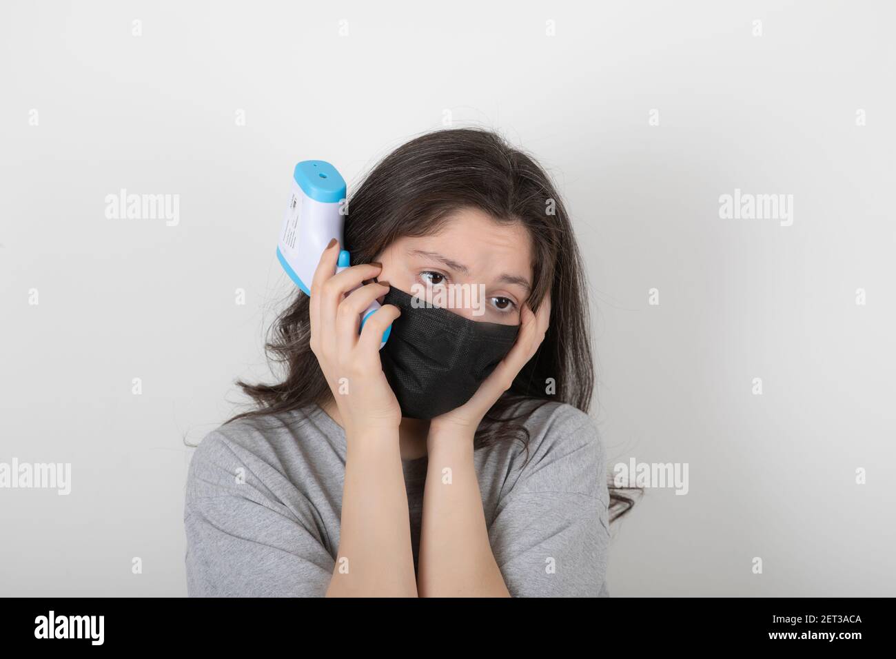 Portrait of young girl in black face mask holding her face on white ...