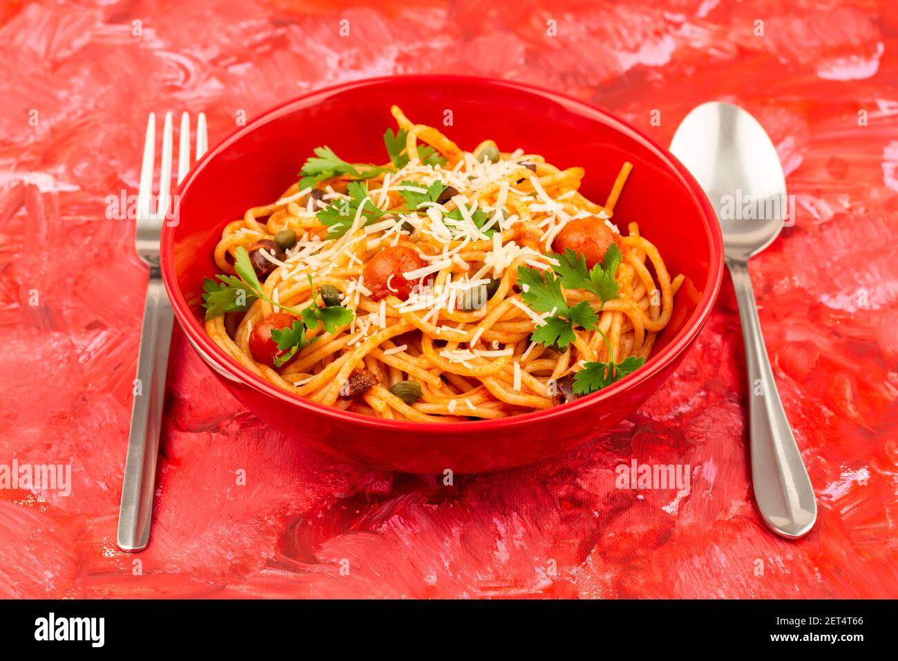 Pasta spaghetti Puttanesca in red bowl with fork and spoon on colorful ...