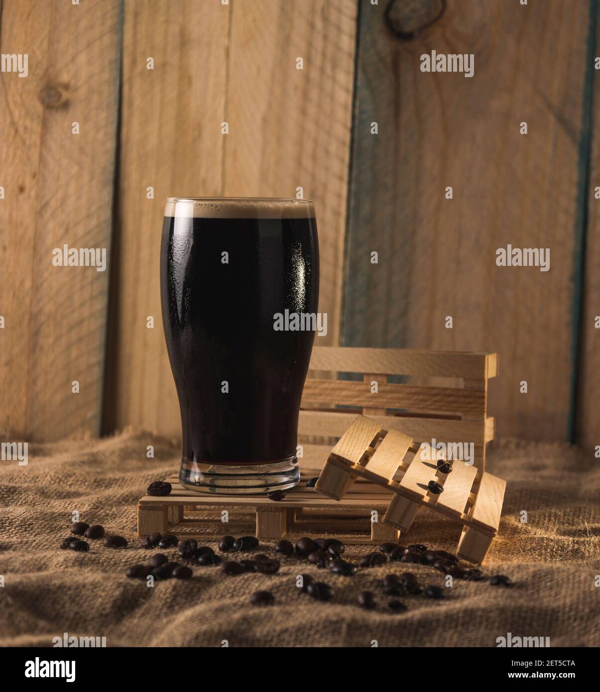 A black beer in a glass with coffee beans with a wooden wall on a ...