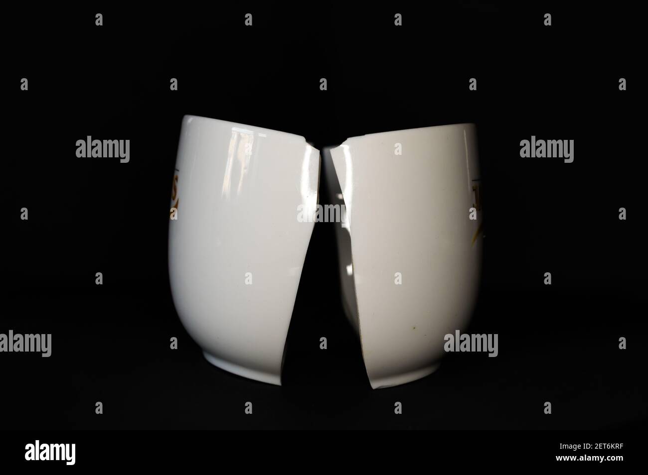 A closeup of a white coffee cup broken in half isolated on a black ...