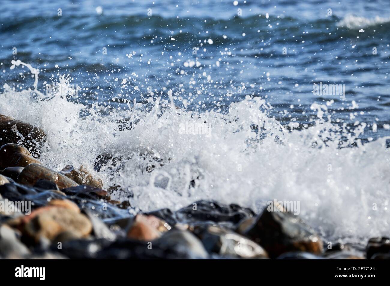 Small wave rolls onto shore and splash of foam flies in different ...