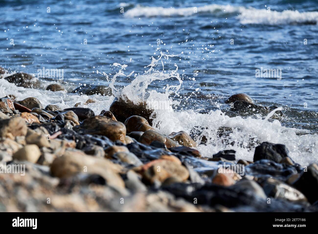 Small wave rolls onto shore and splash of foam flies in different ...
