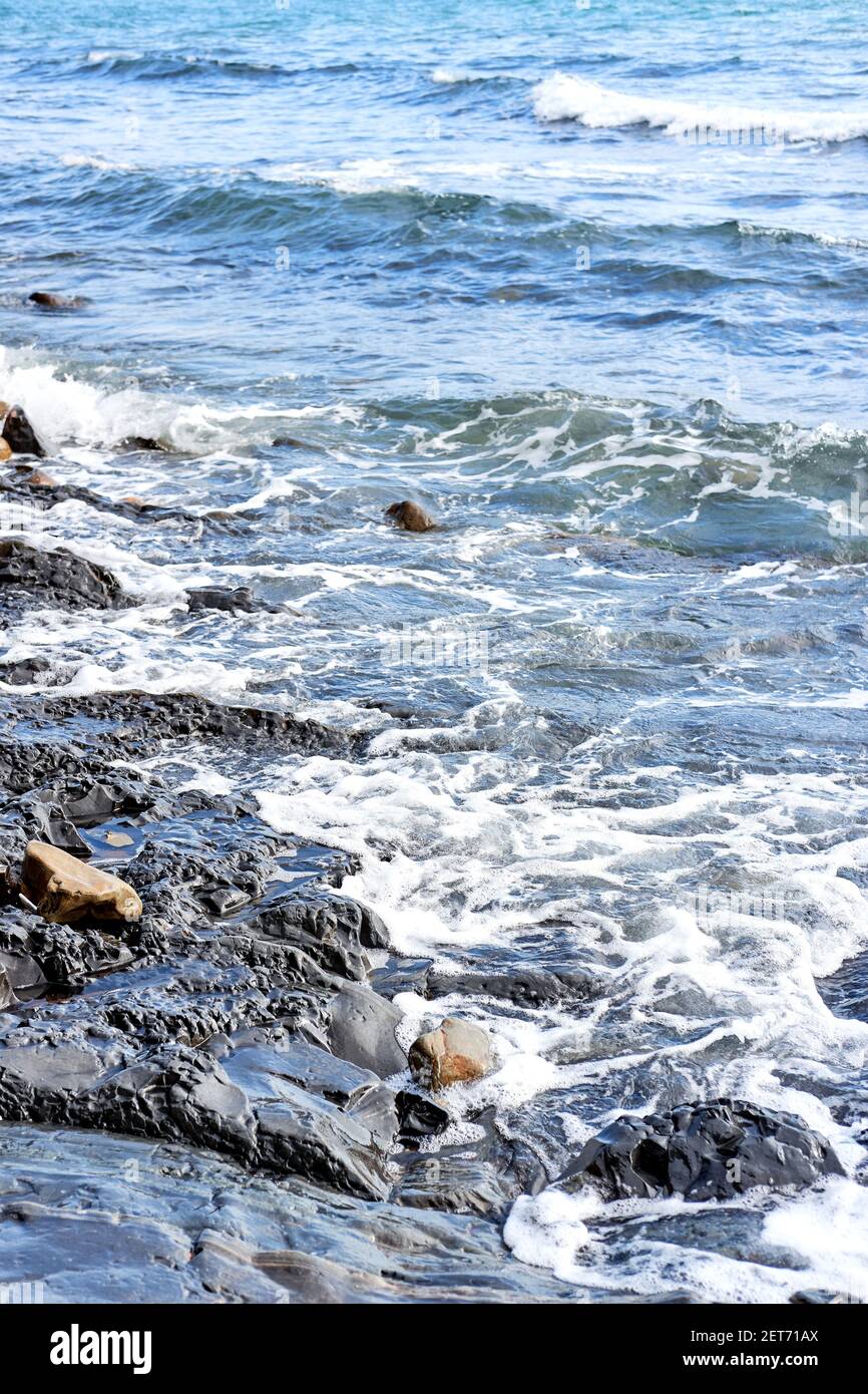 Small wave rolls onto shore and splash of foam flies in different ...