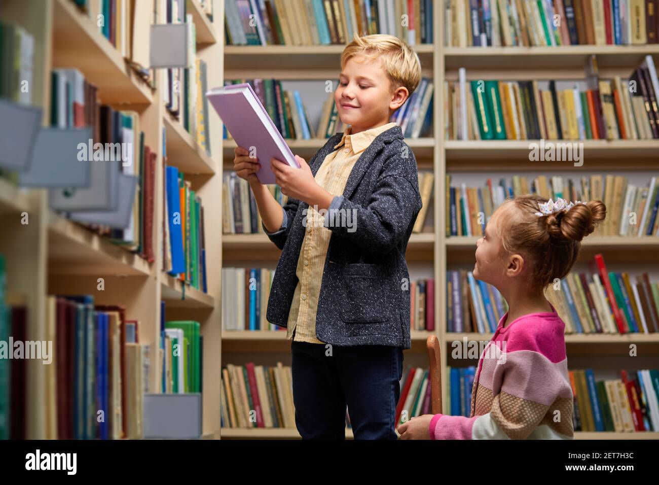 brother and sister choose books in library, having conversation, in ...
