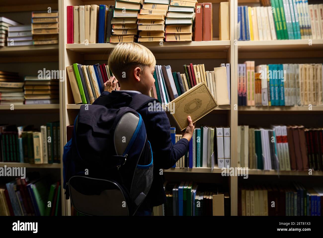 view from back on awesome child boy choosing book in library standing ...