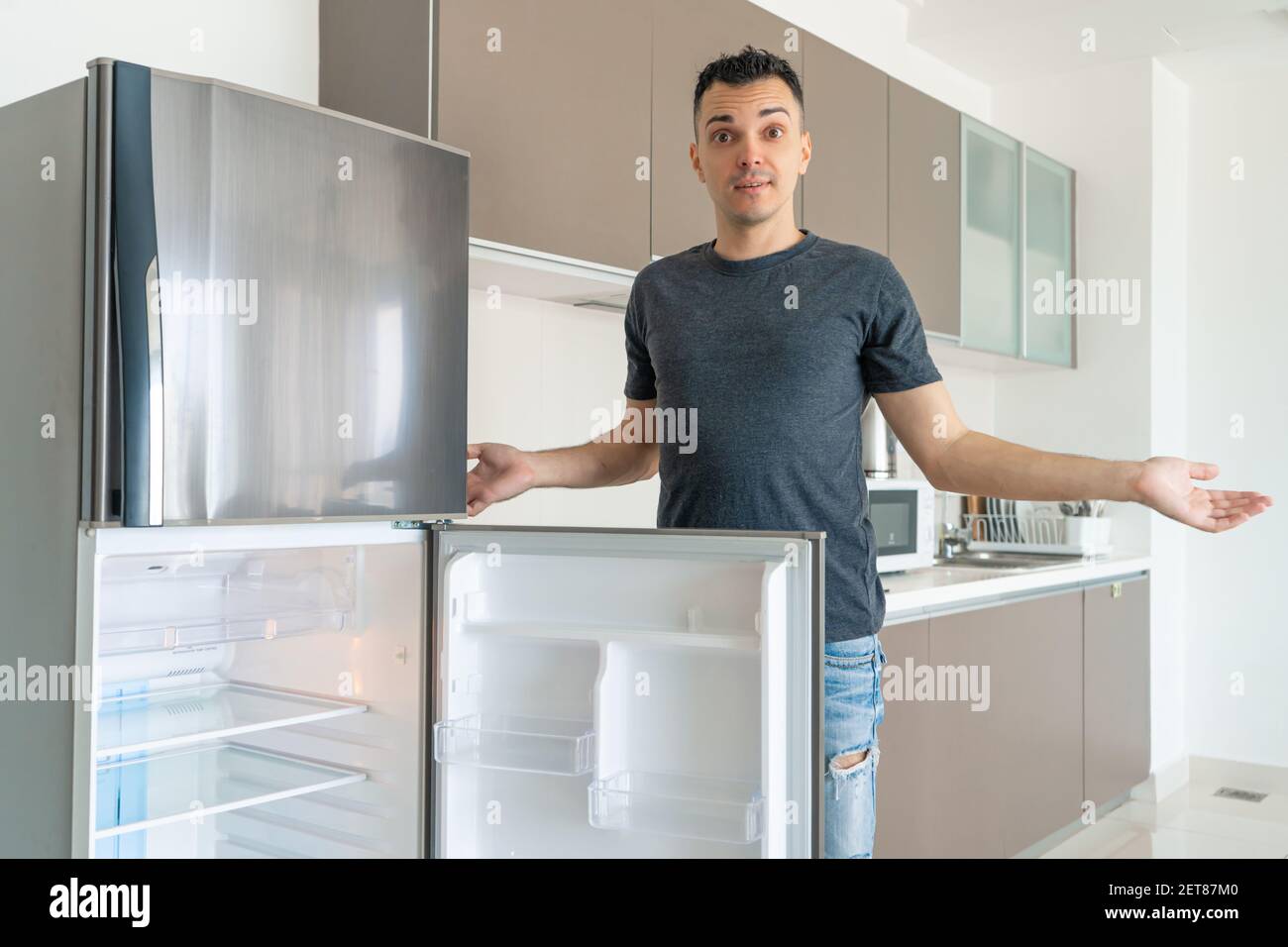 The guy is sad near the empty refrigerator without food. Food delivery ...