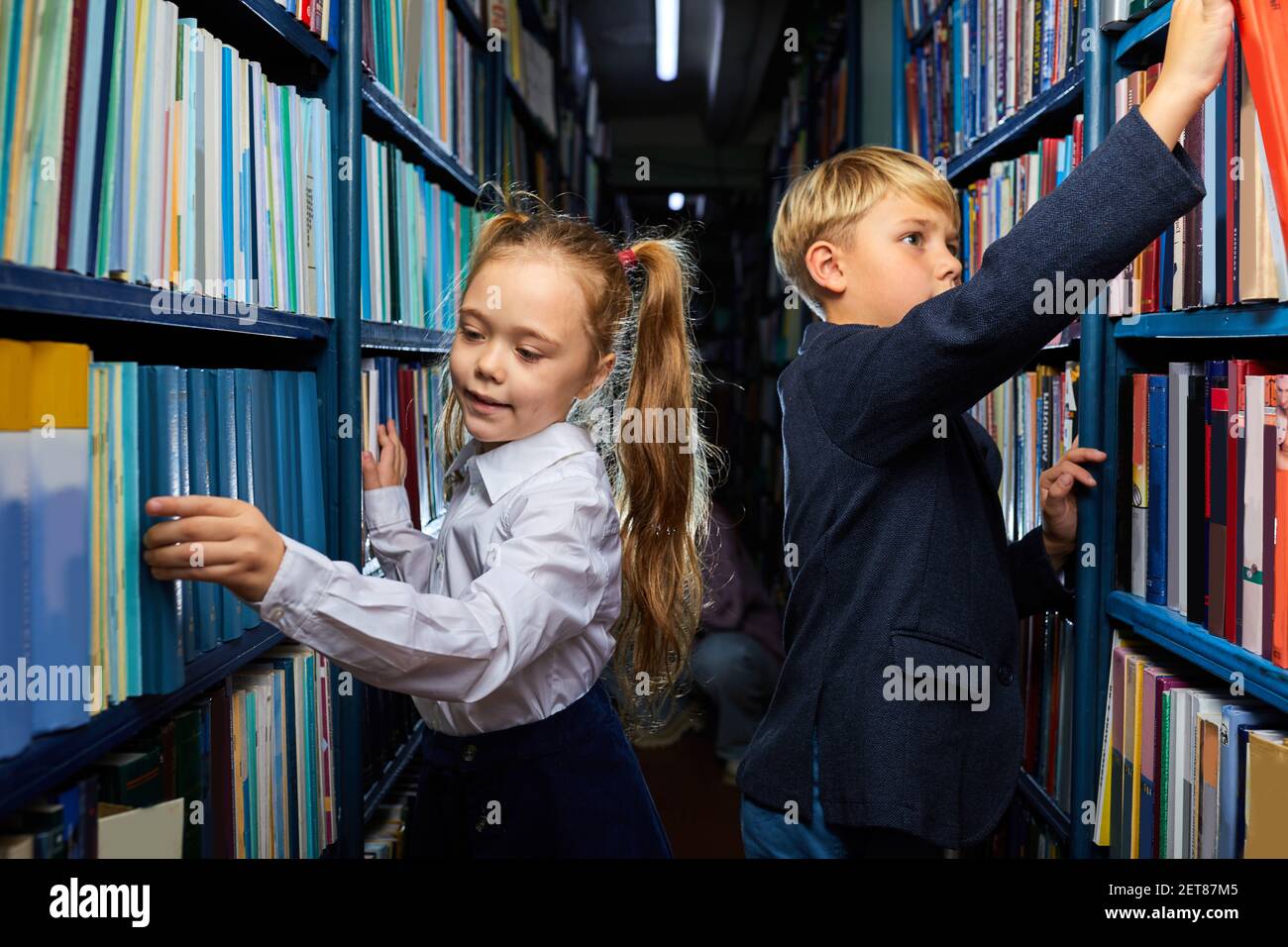 school children in library choosing books standing between shelves back ...