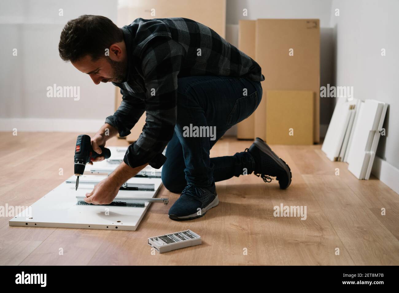 man crouched on the floor assembling a piece of furniture. Do it ...