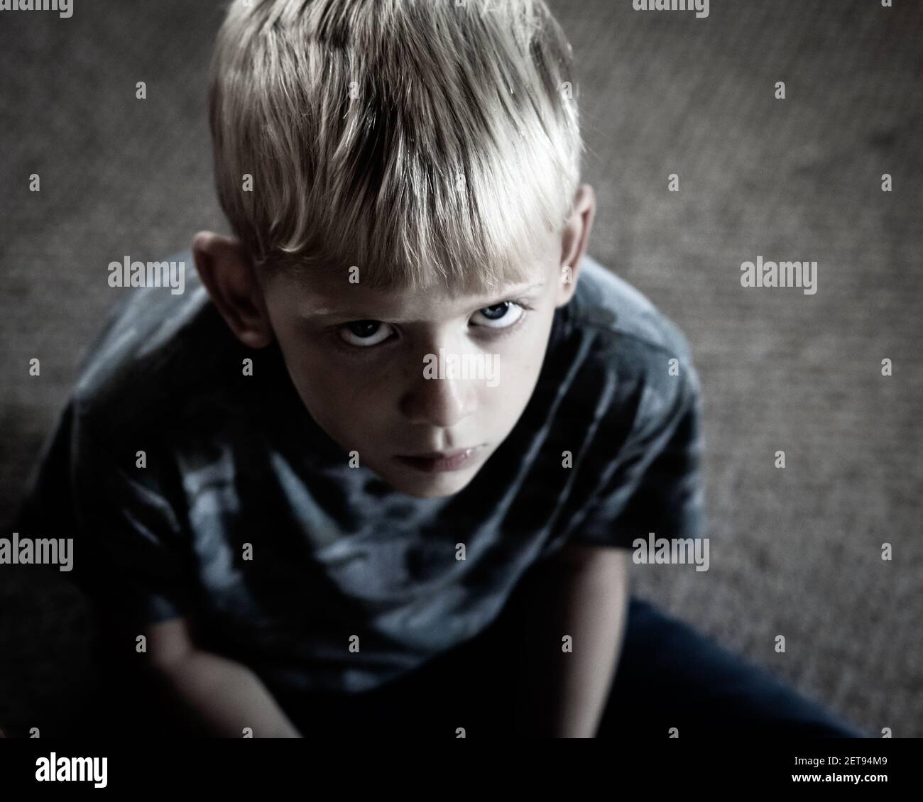 A shallow focus of a lonely scared kid sitting on the floor and looking ...