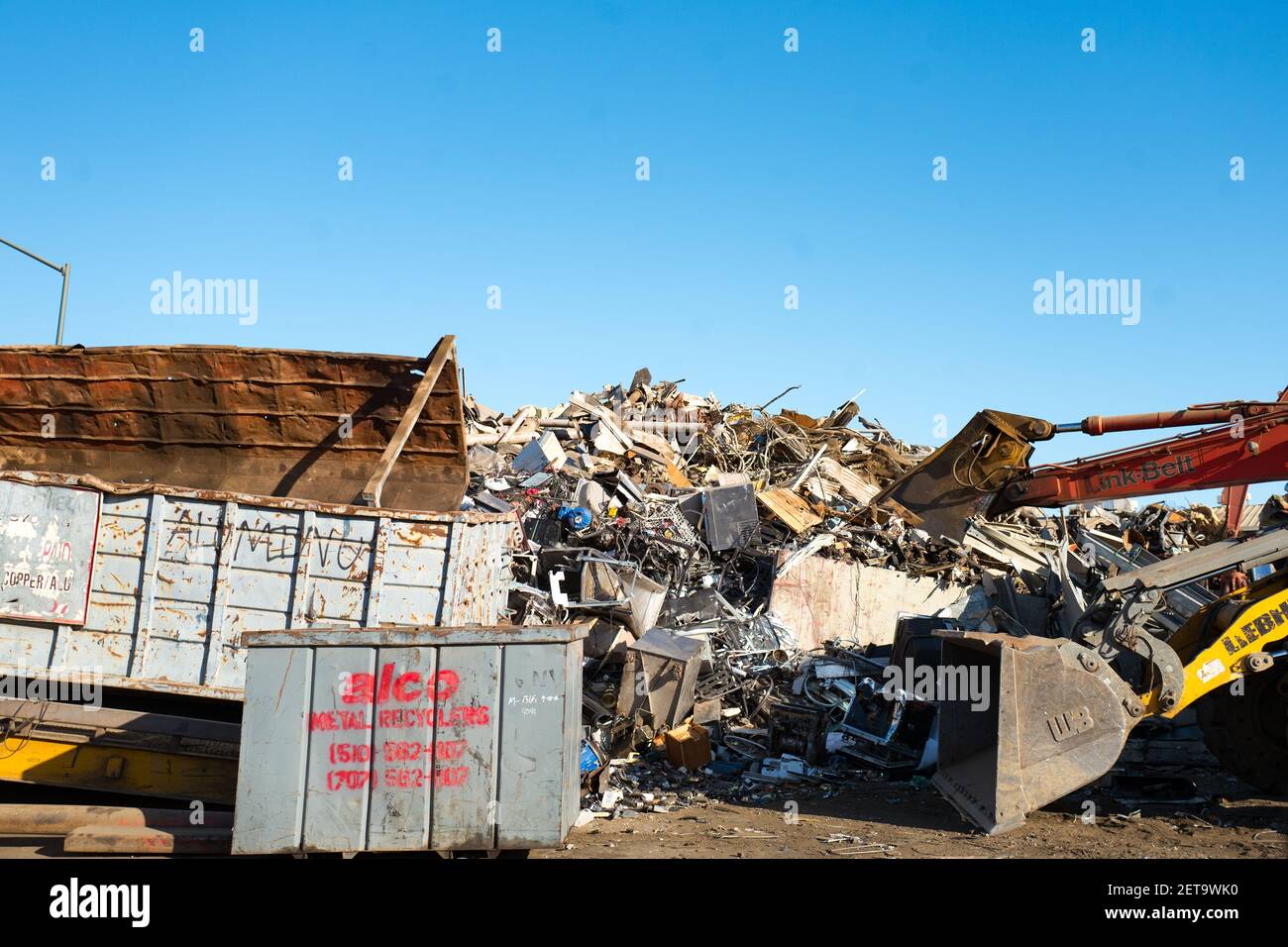 Large piles of scrap metal are visible under bright sun, with a ...