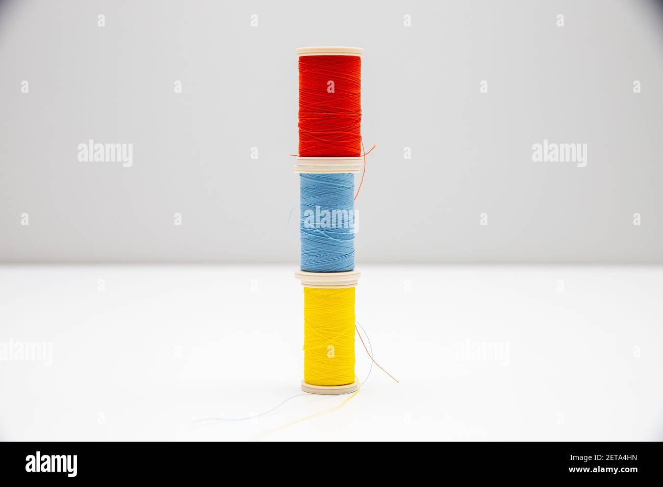 Three thread spools of red, blue, and yellow colors stacked on each ...