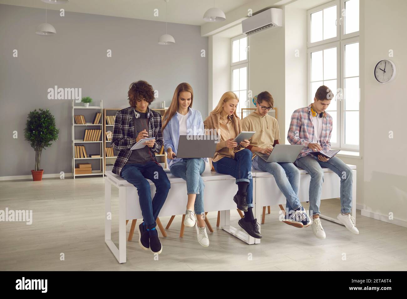 College students sitting in classroom, using devices, reading notes and ...