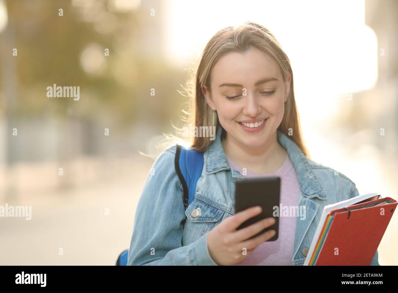 Front view of a happy student checking smart phone walking in the ...