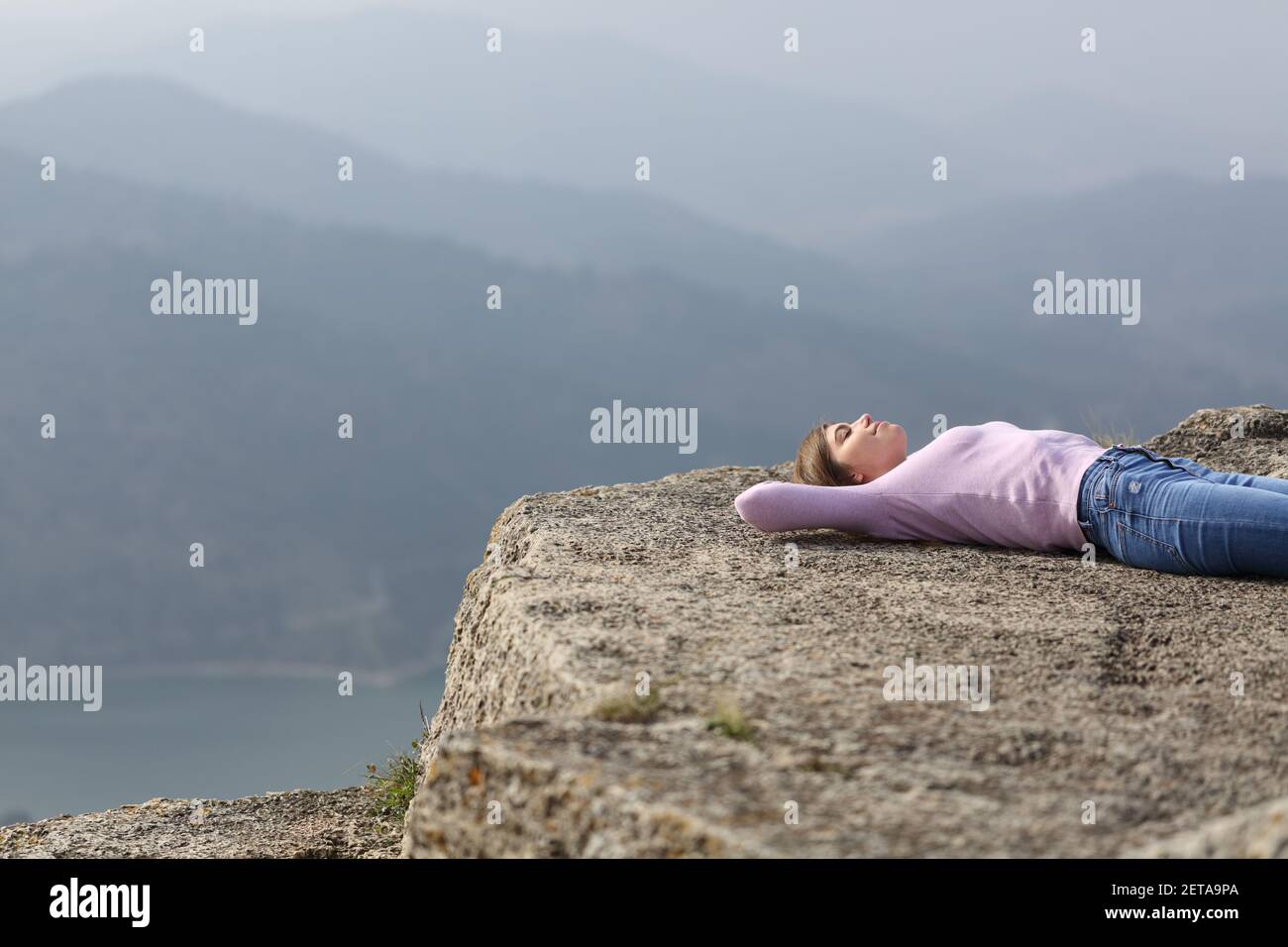 Relaxed woman resting alone lying on the top of a cliff in the mountain ...