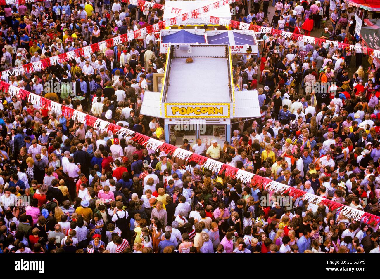 1970s DENSE CROWD OF PEOPLE AROUND POPCORN STAND AT COUNTY FAIR OR ...