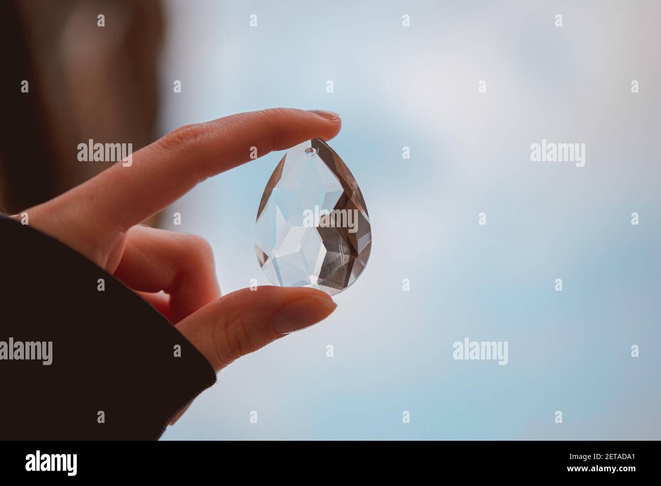 A teardrop-shaped crystal in a female hand in the light blue background ...