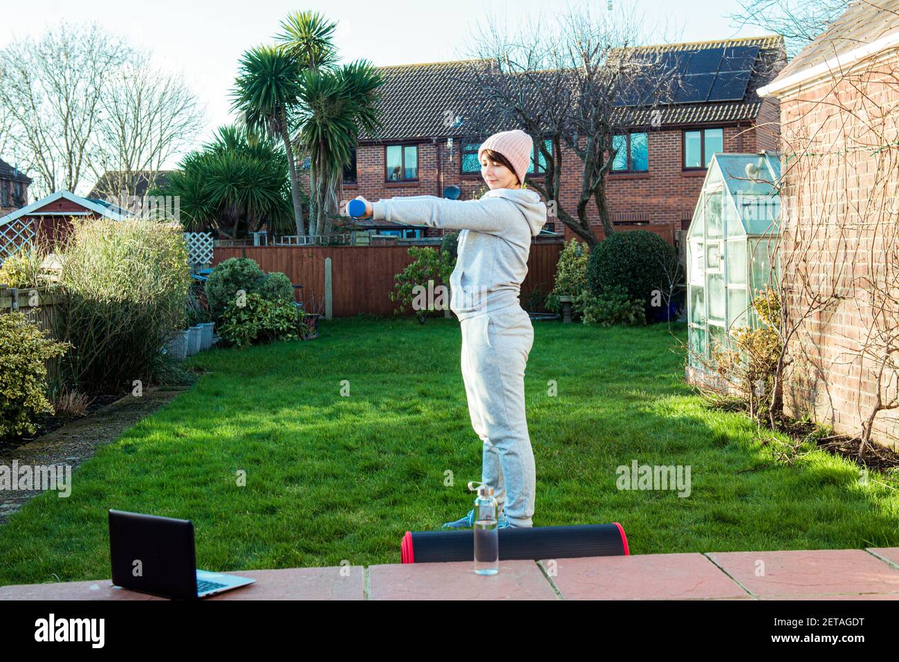 Woman doing sport workout outdoors in her garden, backyard with online ...