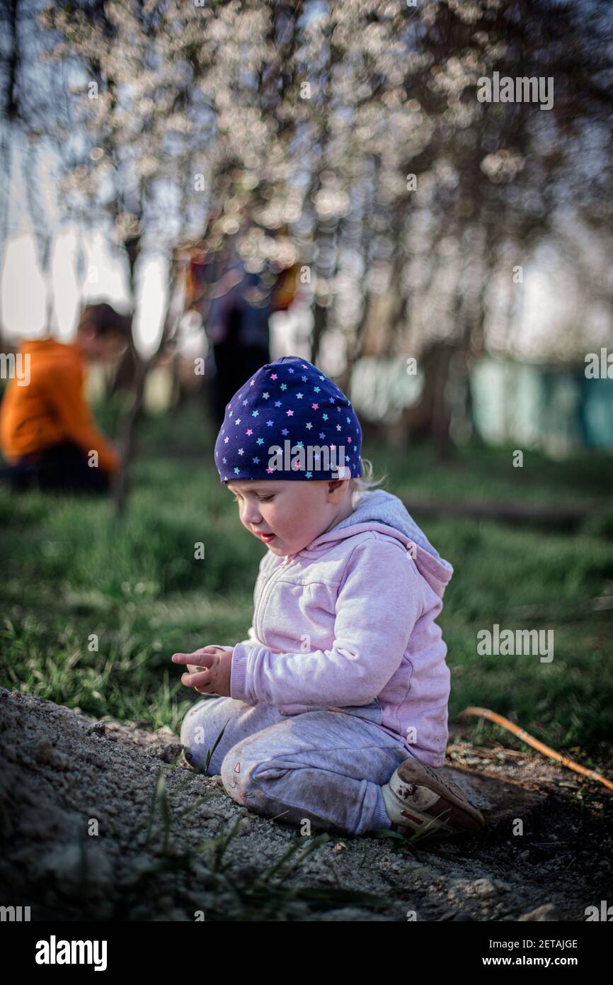 A little girl sits on a pile of soil in the village. A child plays in ...