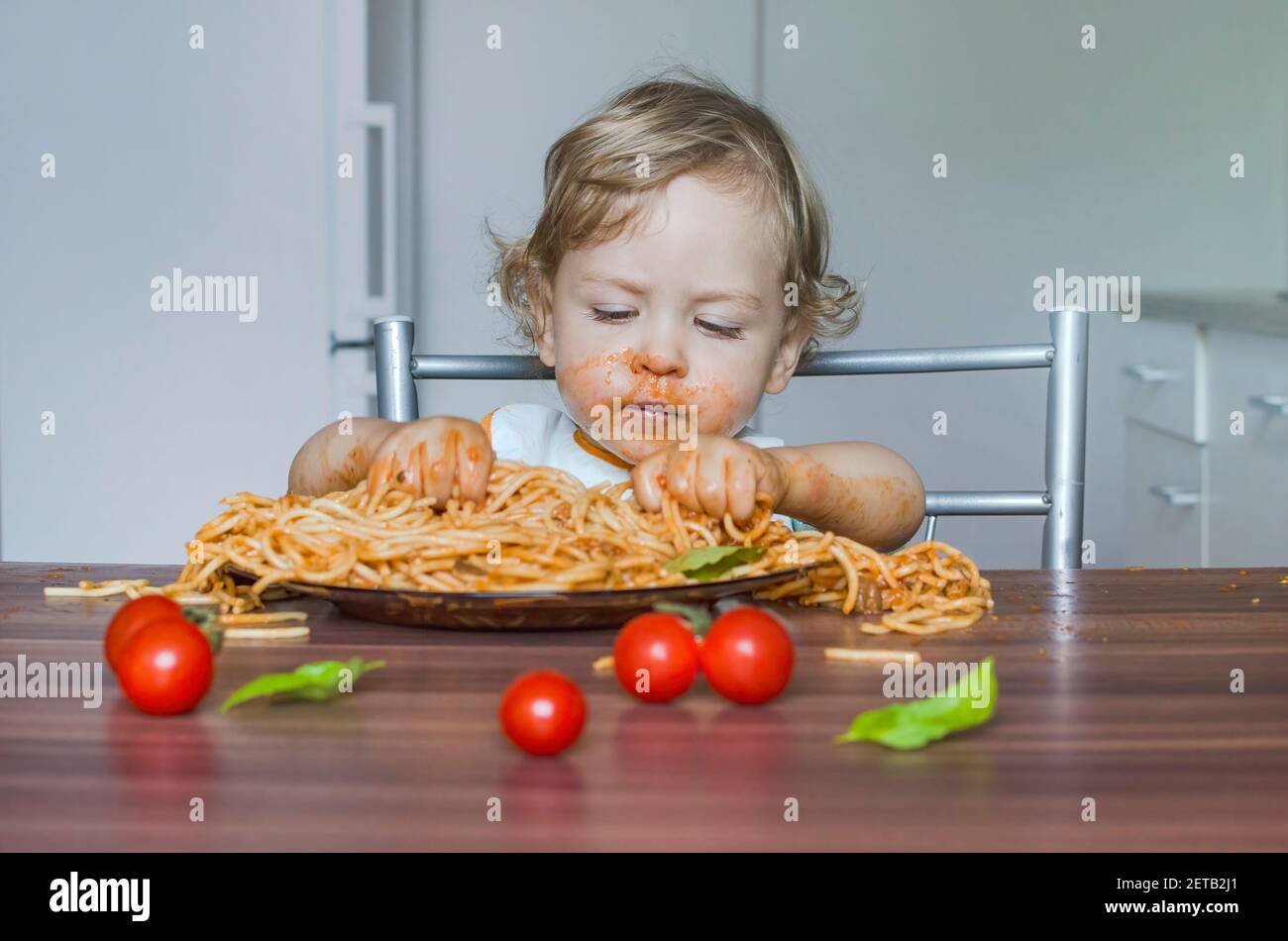 Funny baby child getting messy eating spaghetti with tomato sauce from ...