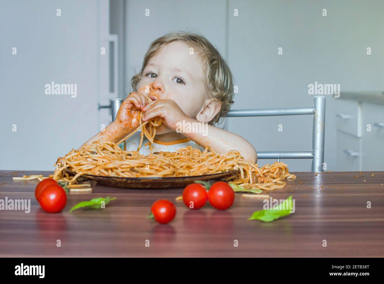 Funny baby child getting messy eating spaghetti with tomato sauce from ...