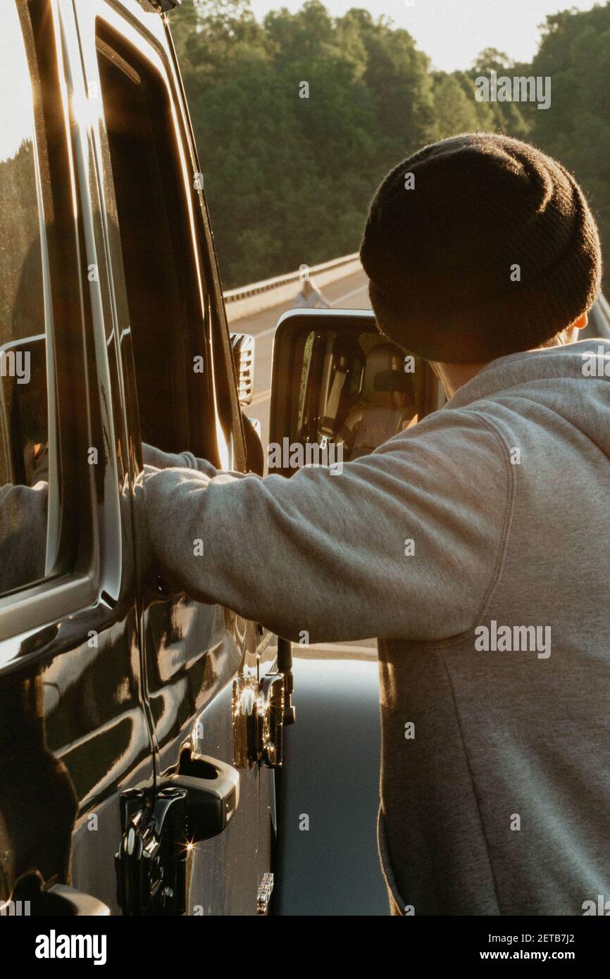 A vertical back view of a male standing outside a car and looking at ...