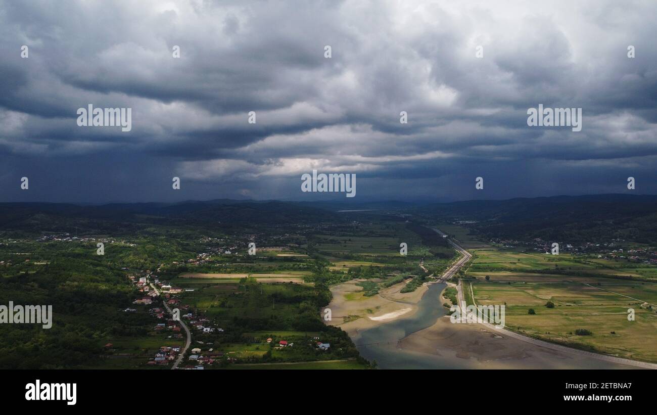 An aerial shot of houses on a greenfield near a river under a gloomy ...