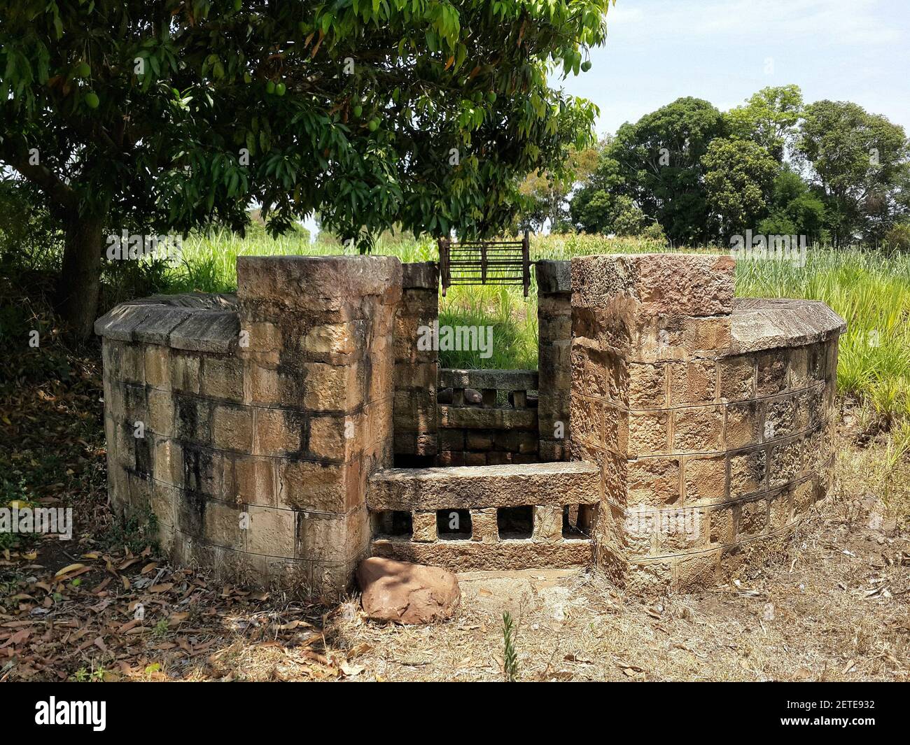 the old water well constructed of stone in the background of field and ...