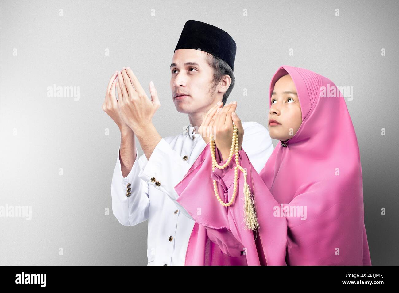 Asian Muslim couple standing while raised hands and praying together ...