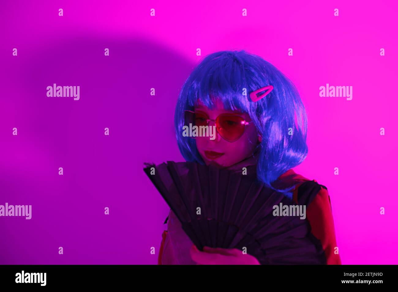 Little girl posing with a fan for a photo shoot on a fuchsia background ...