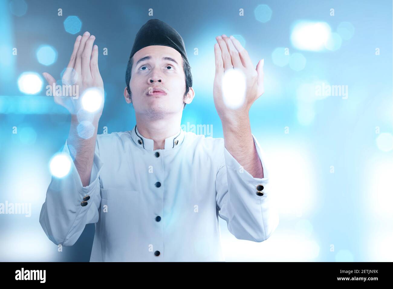 Asian Muslim man standing while raised hands and praying with blurred ...