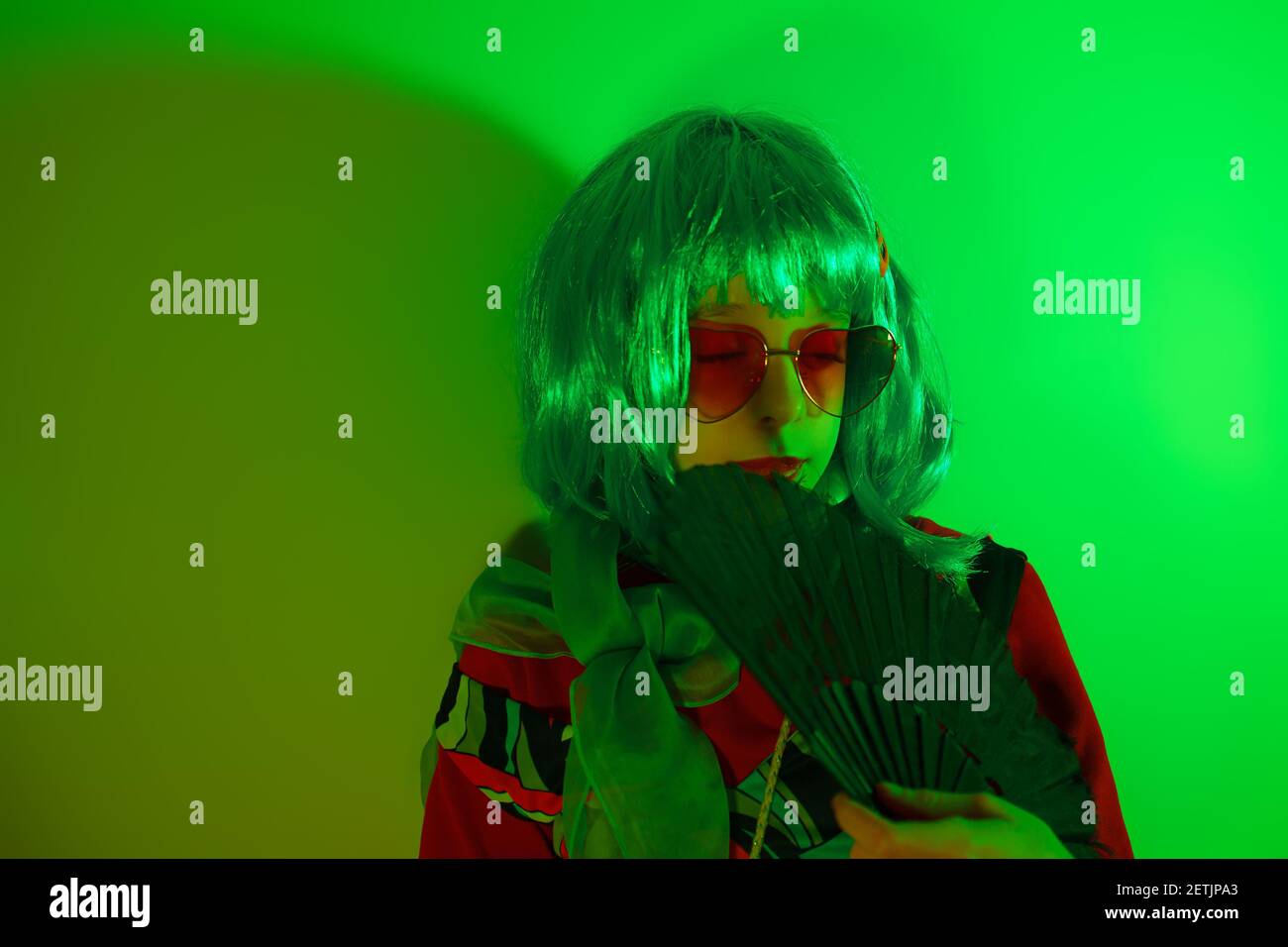 Little girl posing with a fan for a photo shoot on a green background ...