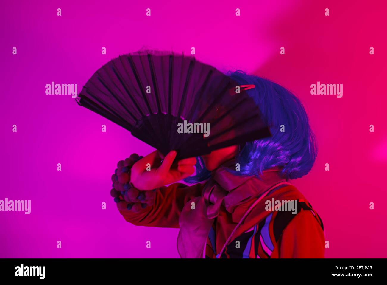 Little girl posing with a fan for a photo shoot on a fuchsia background ...