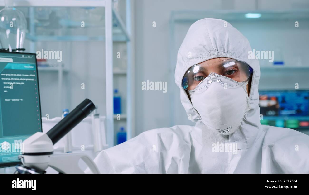 Professional woman scientist in protection suit looking tired at camera ...