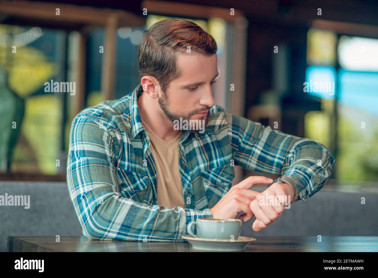 Serious man looking at watch sitting in cafe Stock Photo - Alamy